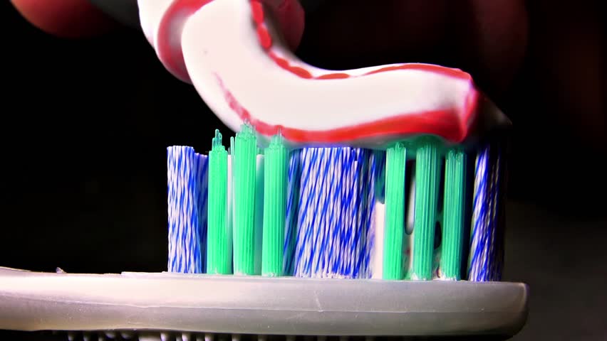 Toothpaste being squeezed on to a toothbrush on black background, side ...